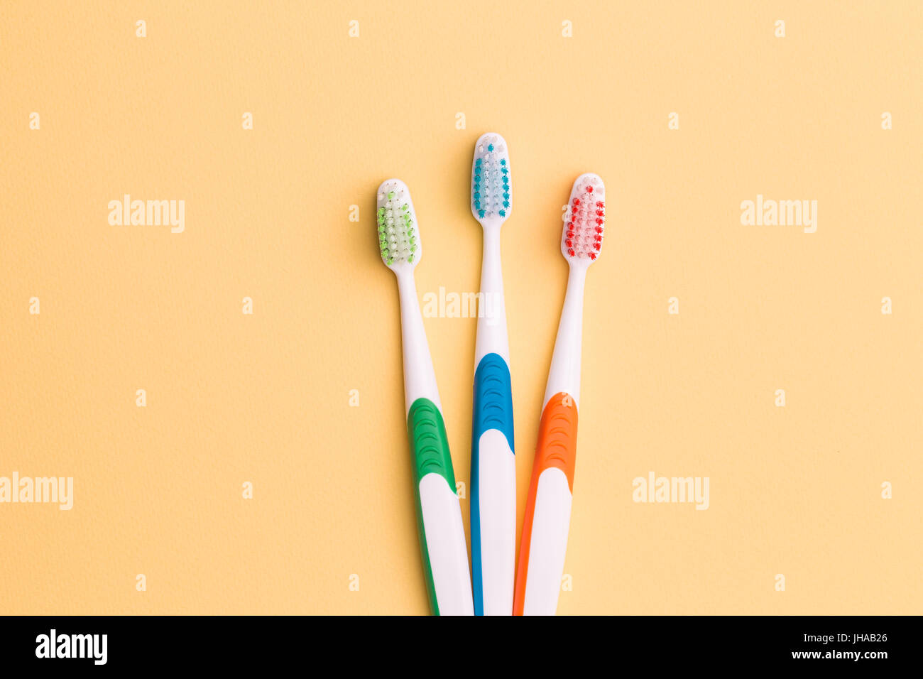 Photo of three multi-colored toothbrushes on empty orange background ...