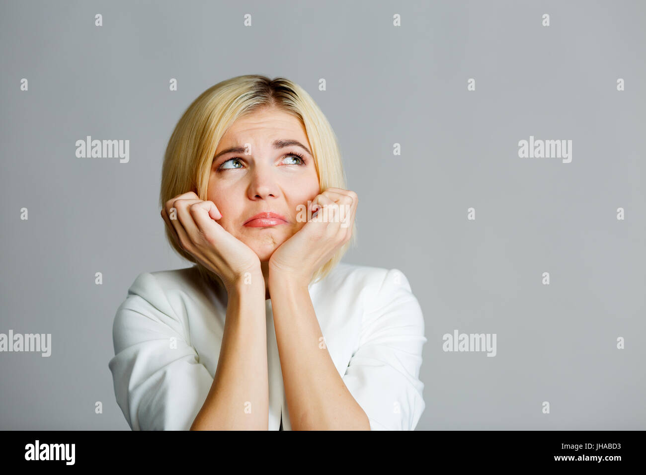 Sad model with hand at chin on empty gray background Stock Photo - Alamy