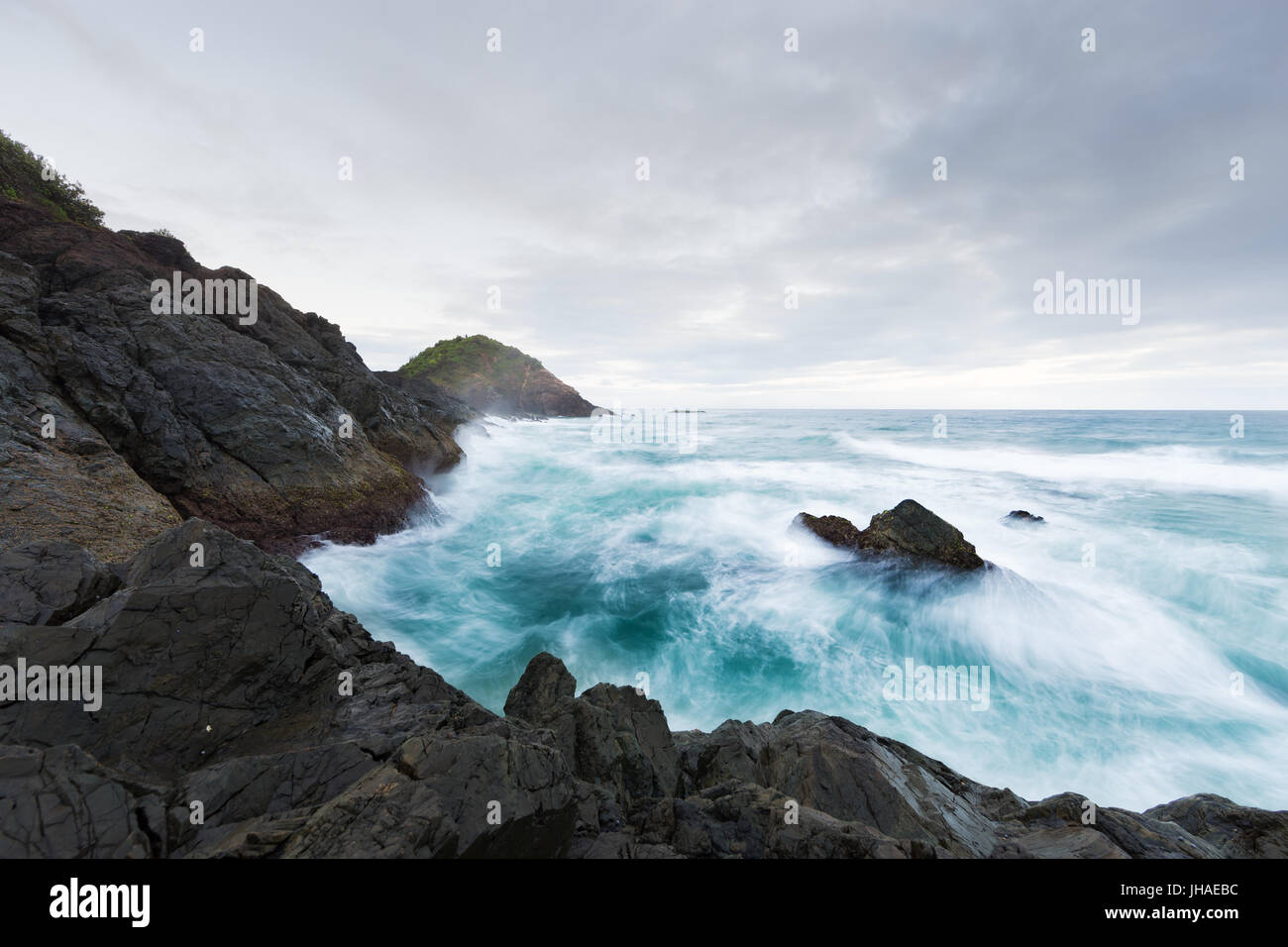 A rough, luminous blue ocean washes around a rocky headland under a ...