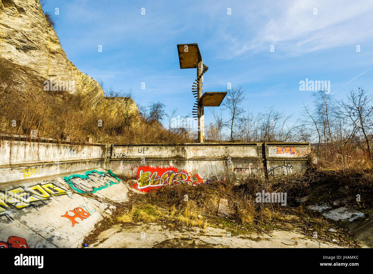 empty old overgrown run-down swimming pool with jumping tower, part of ...