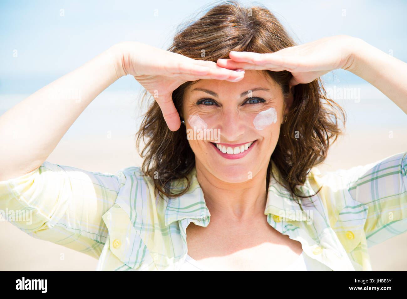 Funny middle aged woman applying sunscreen lotion on face on the beach ...