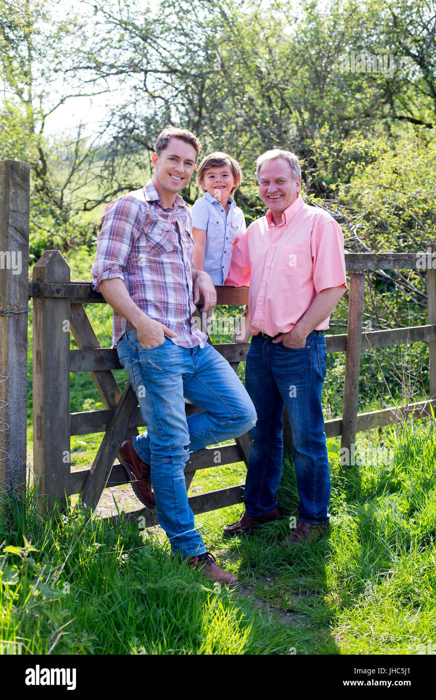 A little boy is sitting on a farm gate in the countryside with his ...