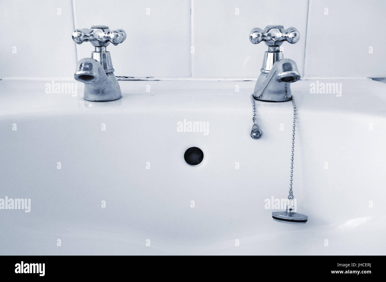 A pair of silver taps on a white sink with a plug on a chain Stock ...