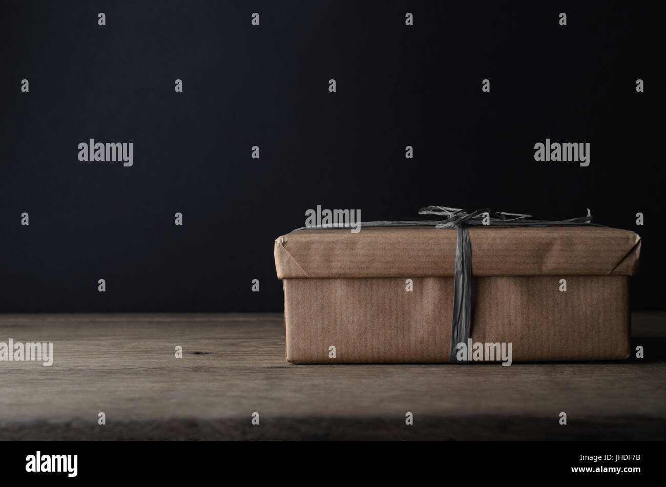 A gift box, in plain brown paper wrapping with dark grey raffia ribbon ...