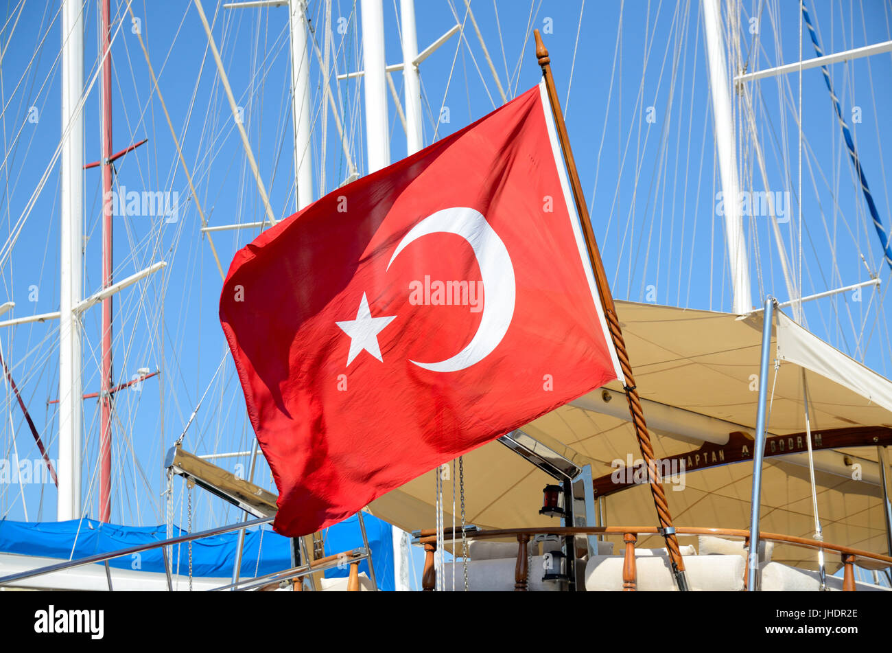 Bodrum port, Turkey. Big Turkish flag on ship, behind masts and blue ...