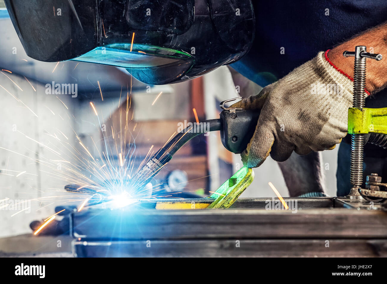 Close-up A young man welder wearing a black welding mask weld a metal ...