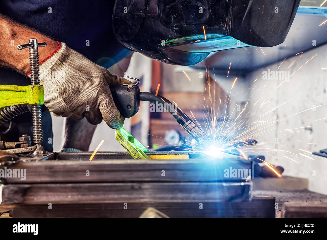 Close-up A young man welder wearing a black welding mask weld a metal ...