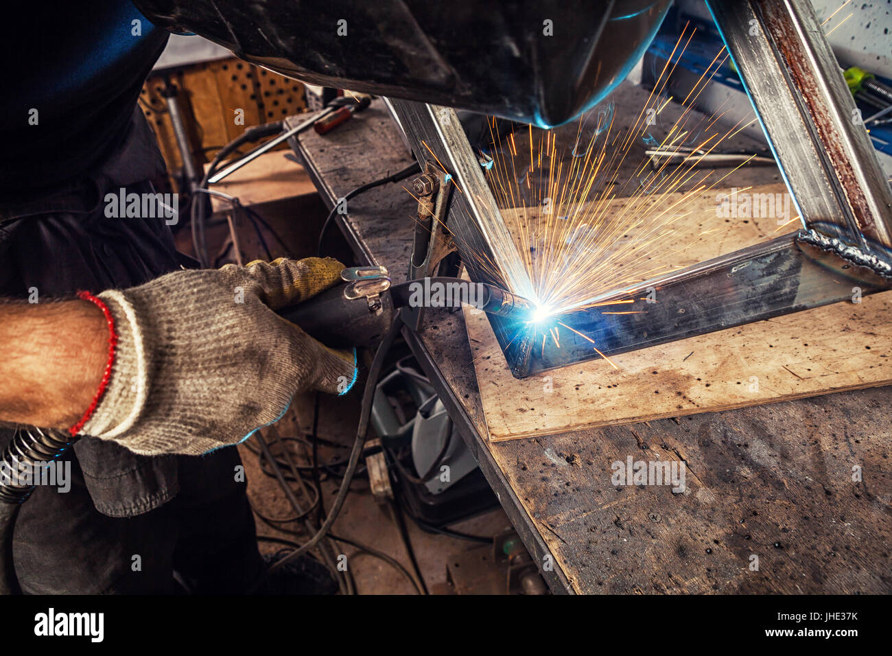 A young man welder in a welding mask and construction gloves, weld a ...