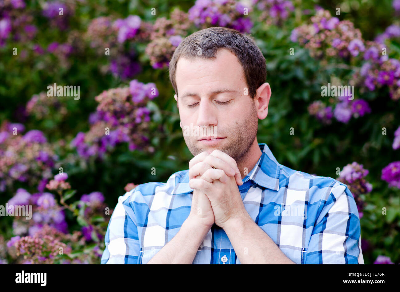 Close up of man praying alone outside with eyes closed and hands ...
