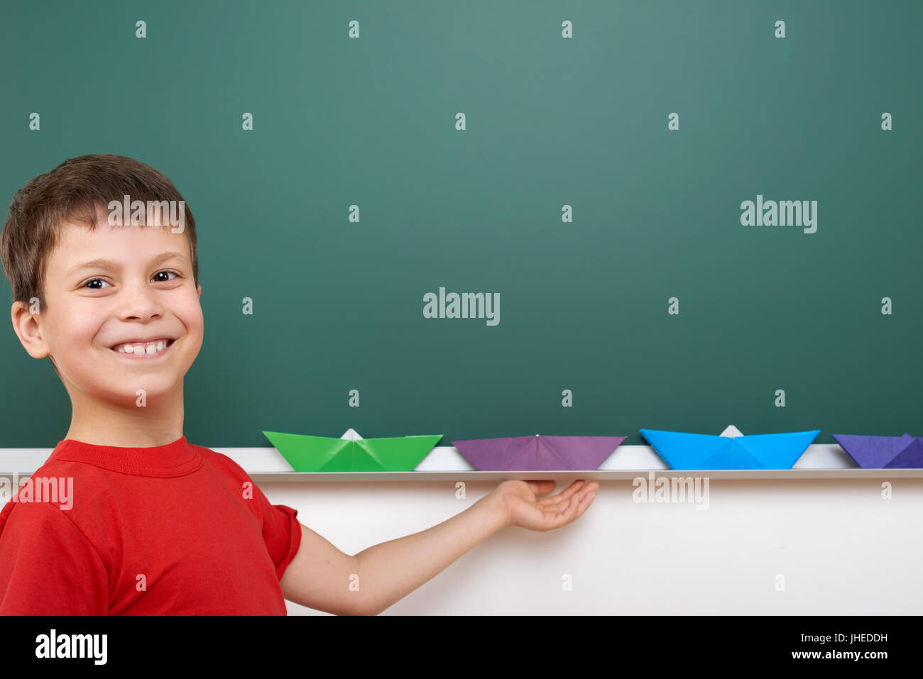 Schoolboy with paper boat play near a blackboard, empty space ...