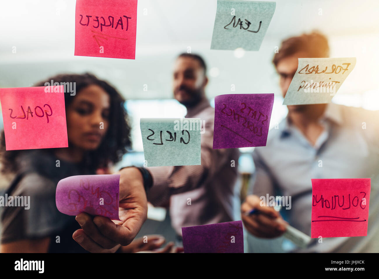 Business people writing on sticky notes and sticking them on glass in ...