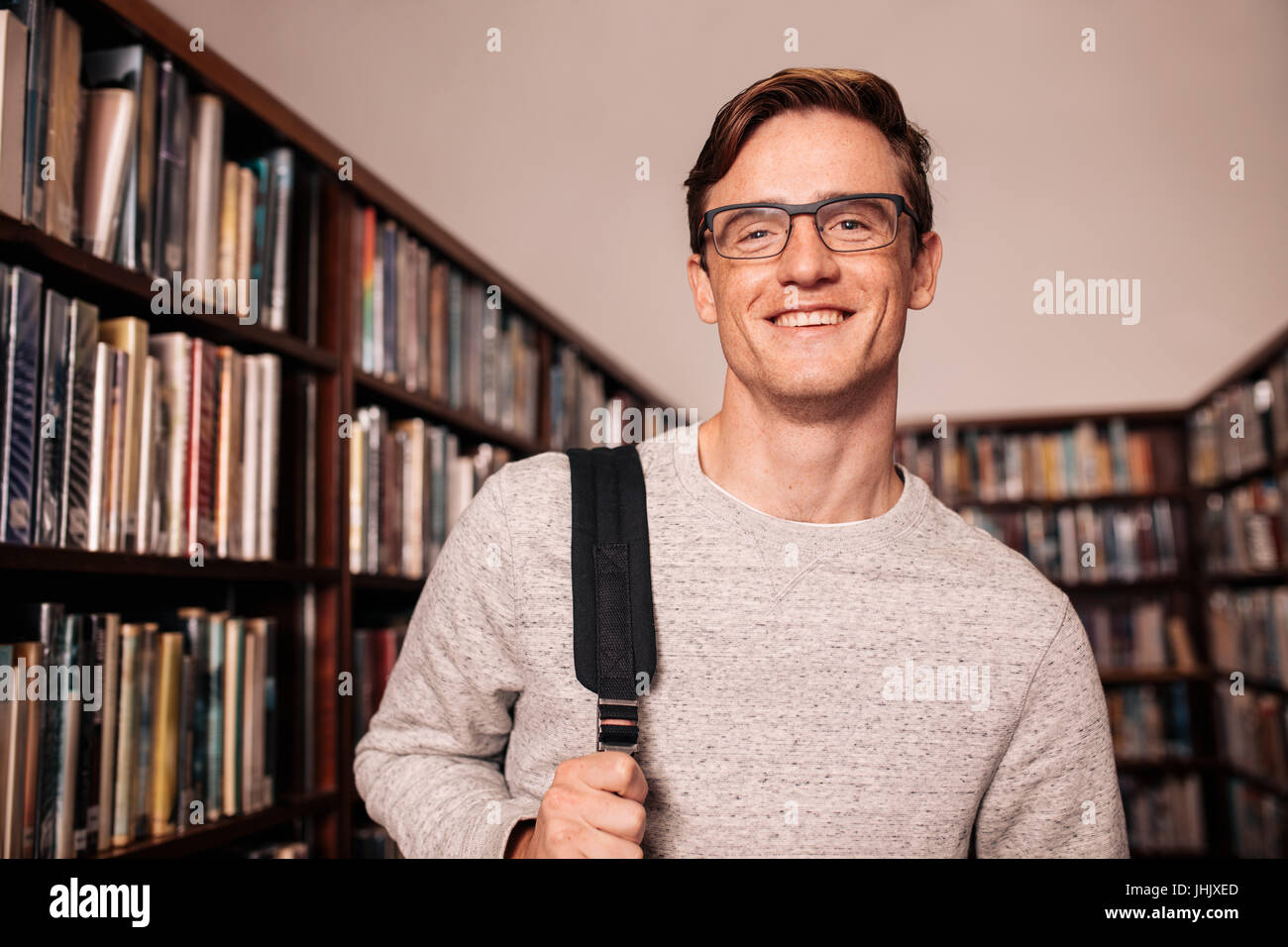 Portrait of young college student standing in library. Smiling ...