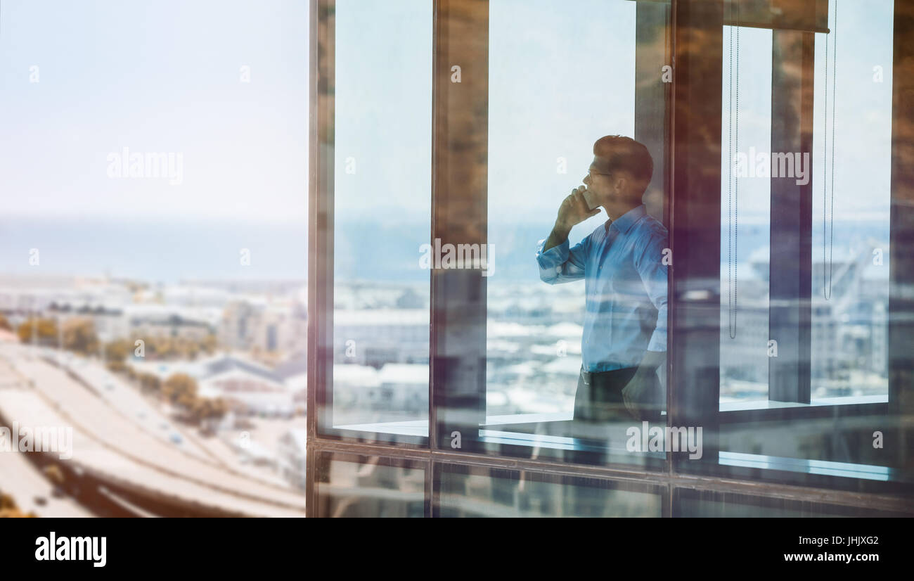 Businessman standing by window and talking on mobile phone. Man ...