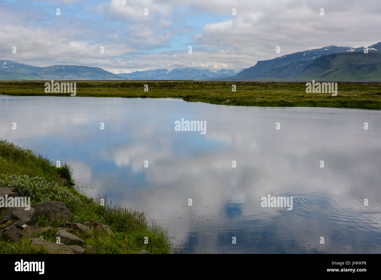Beautiful cloudy sky reflecting in calm water with fresh green field ...