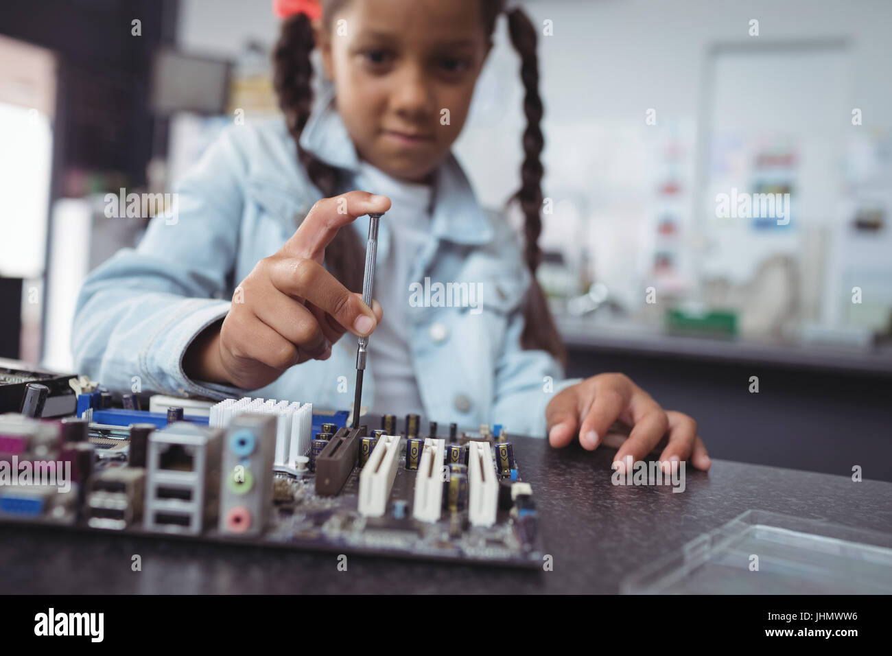 Elementary girl assembling circuit board on desk at electronics lab ...