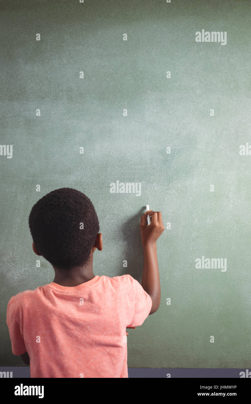 Rear view of boy writing with chalk on greenboard in classroom Stock ...