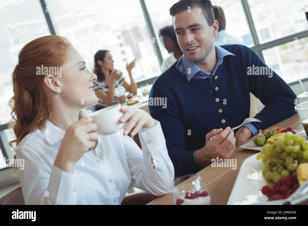 Young business colleagues talking at breakfast table in office ...