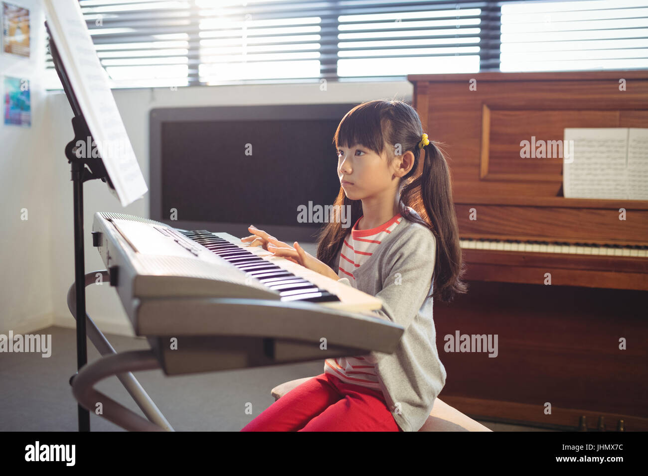 Concentrated girl looking at notes while practicing piano in music ...
