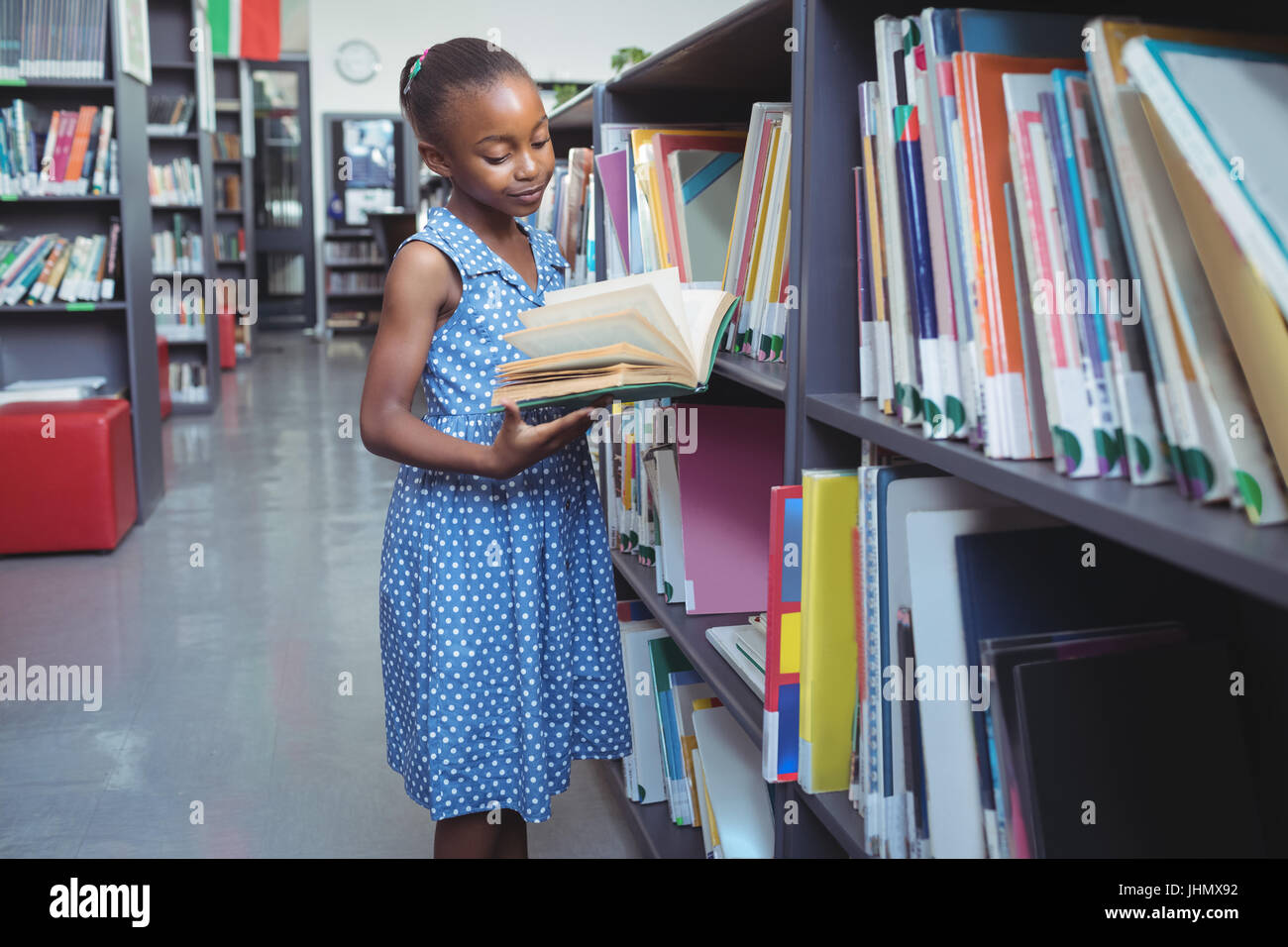 Girl reading book while standing by shelf in library Stock Photo - Alamy