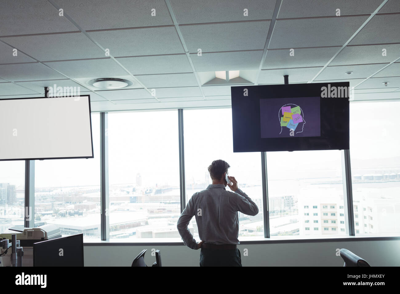 Rear view of businessman taking on mobile phone against glass windows ...