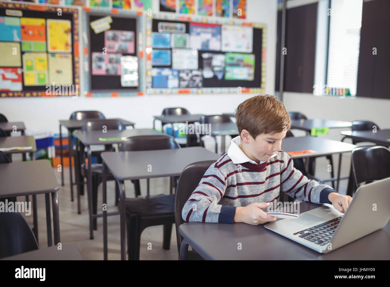 Schoolboy using laptop and mobile phone on desk at classroom Stock ...