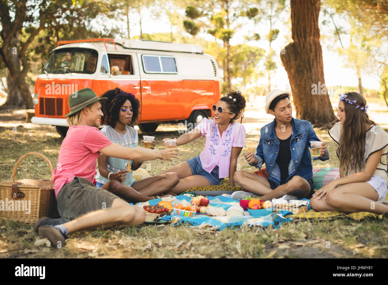 Friends enjoying picnic while sitting against camper van on field Stock ...
