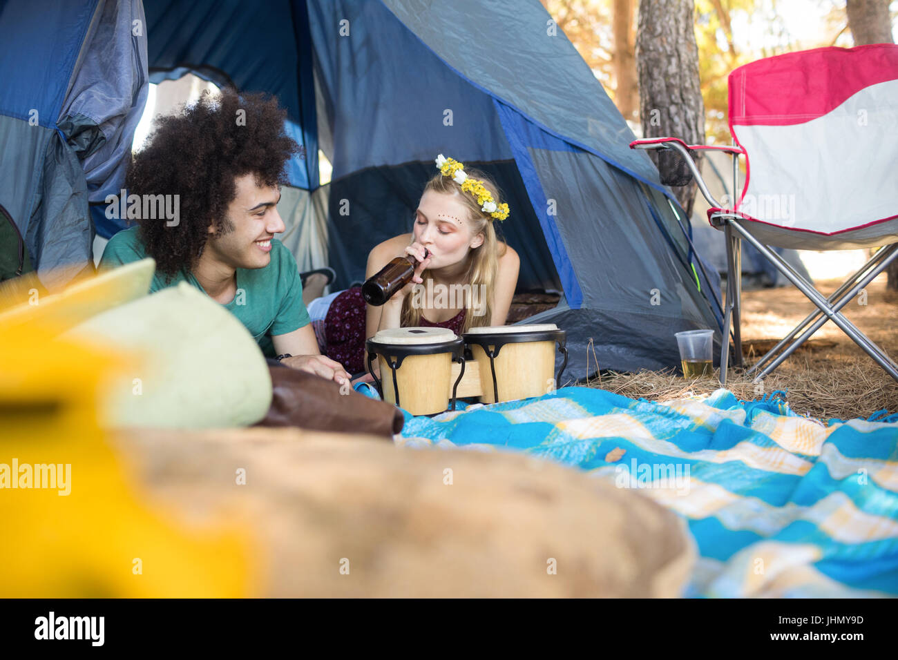 Woman having drink while relaxing with boyfriend in tent at campsite ...