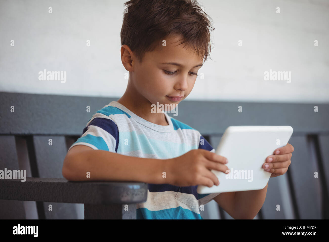 Boy using digital tablet while sitting on bench at school Stock Photo ...