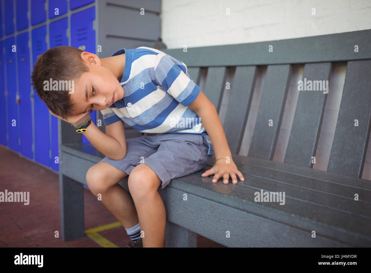 Thoughtful elementary boy sitting on bench in corridor at school Stock ...