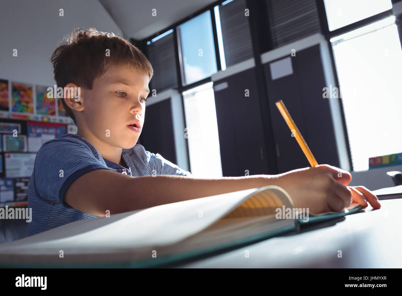 Boy writing on book at desk in classroom Stock Photo - Alamy