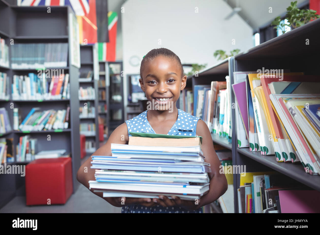 Portrait of smiling girl carrying books by shelf in library Stock Photo ...