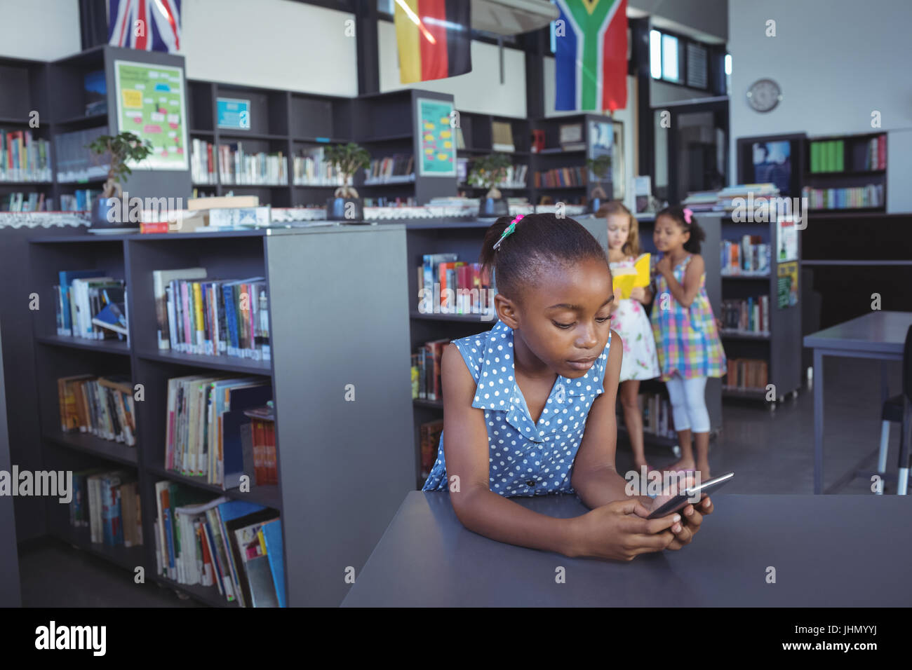 Girl using cellphone while sitting at desk in library Stock Photo - Alamy