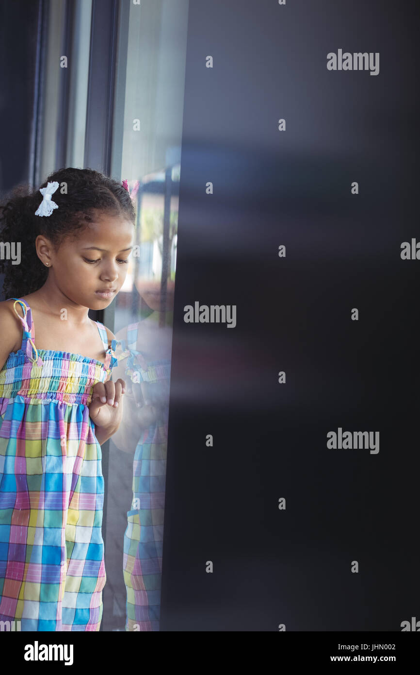 Thoughtful girl looking down while standing by window in school Stock ...