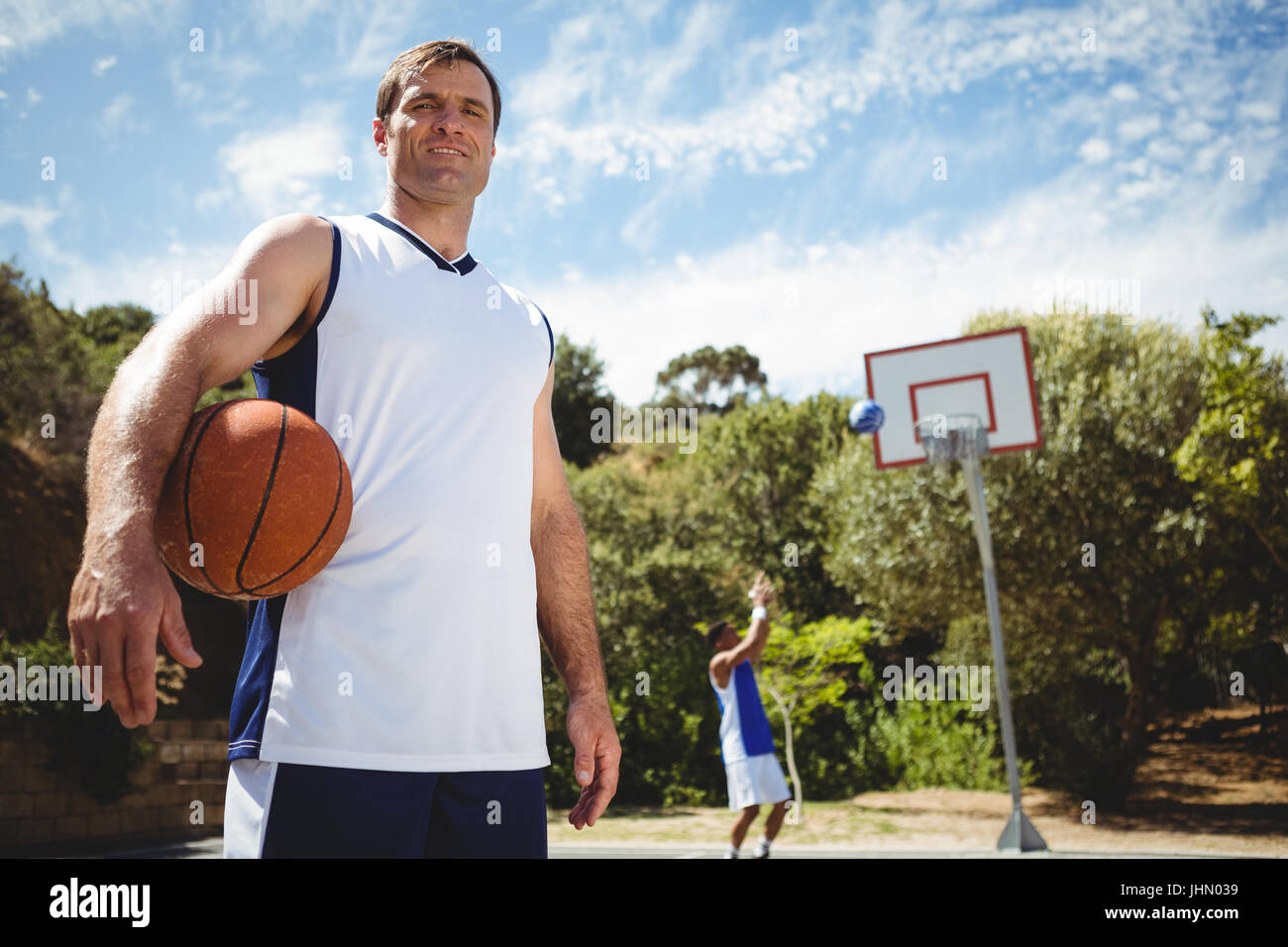 Portrait of man with basketball with friend playing in background at ...