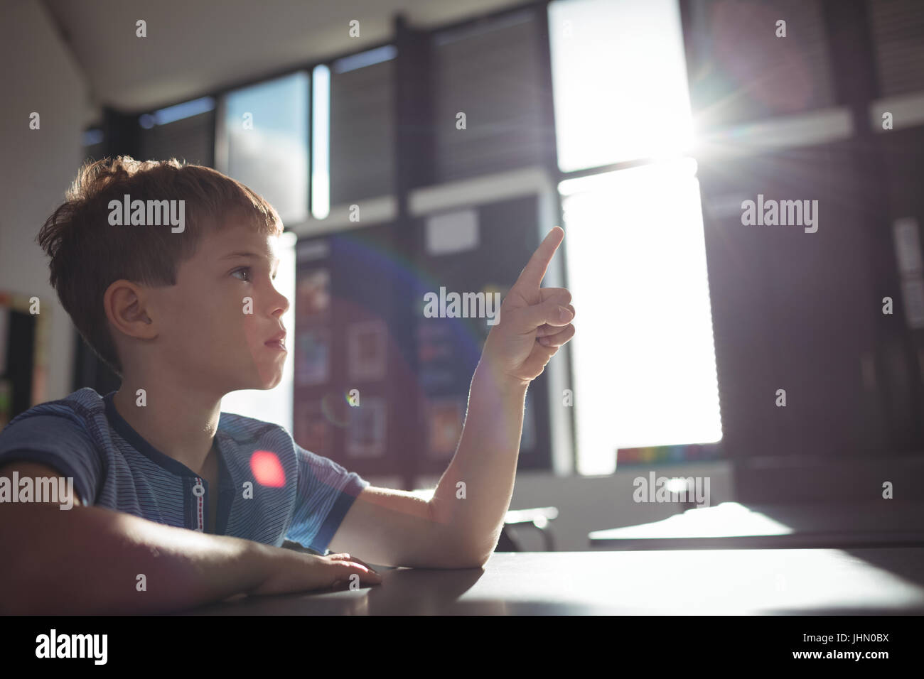 Boy pointing while sitting at desk in school Stock Photo - Alamy