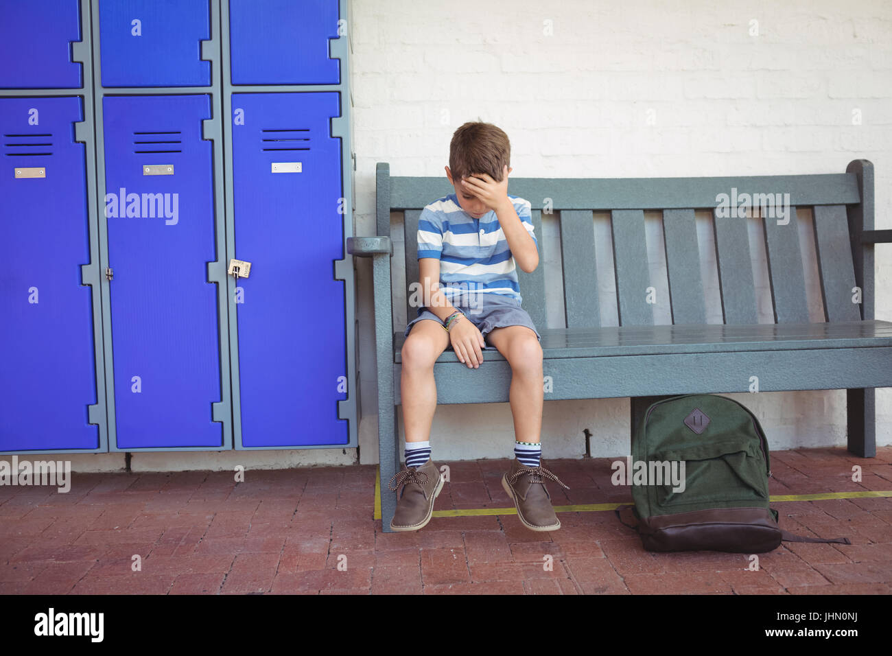 Full length of sad boy sitting on bench by lockers at school Stock ...