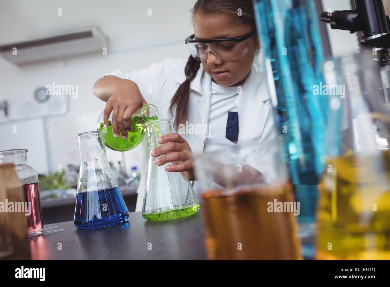 Elementary student pouring green chemical in flask on desk at science ...