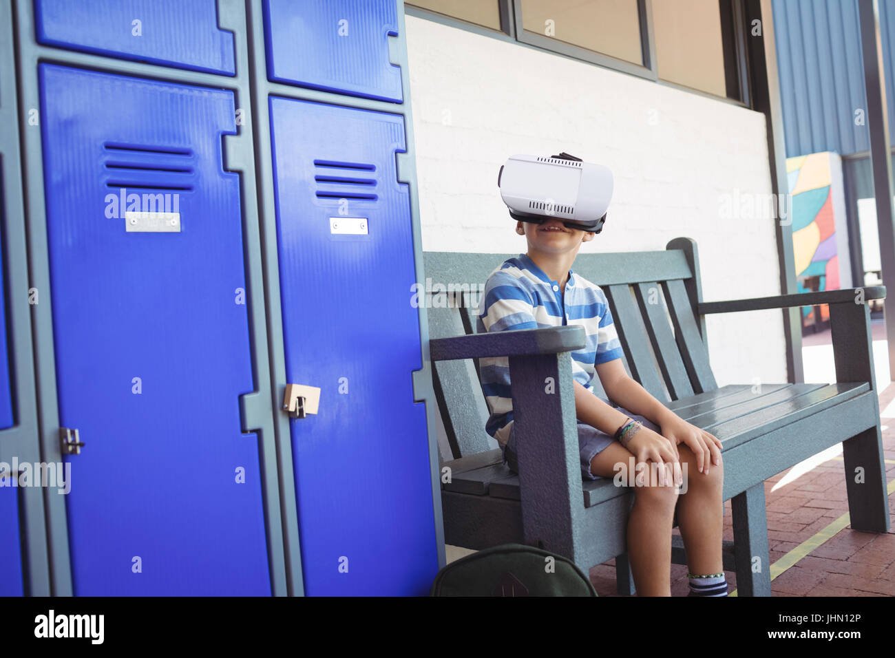 Boy using virtual reality glasses while sitting on bench by lockers in ...