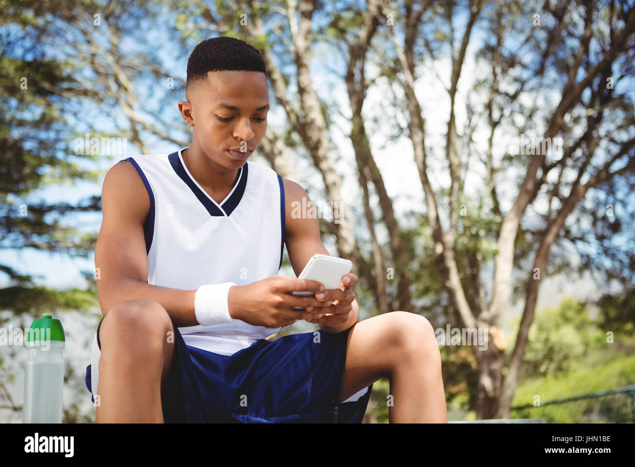 Teenage boy using smart phone while sitting on bench in court Stock ...