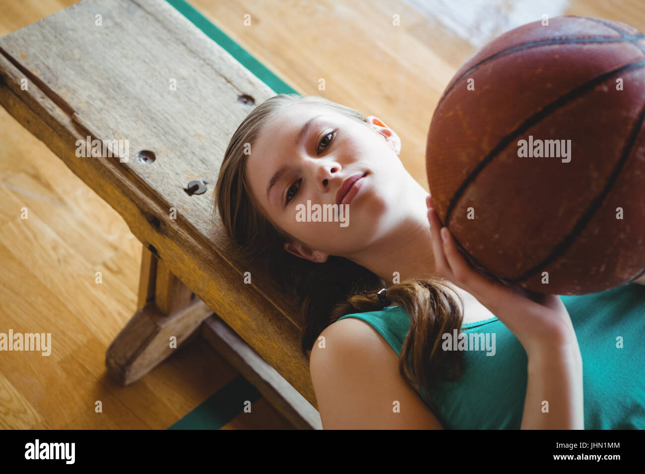 High angle portrait of woman with basketball lying on bench in court ...