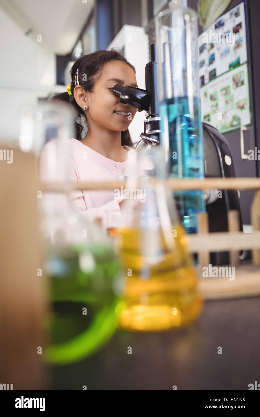 Elementary girl student using microscope on desk at science laboratory ...
