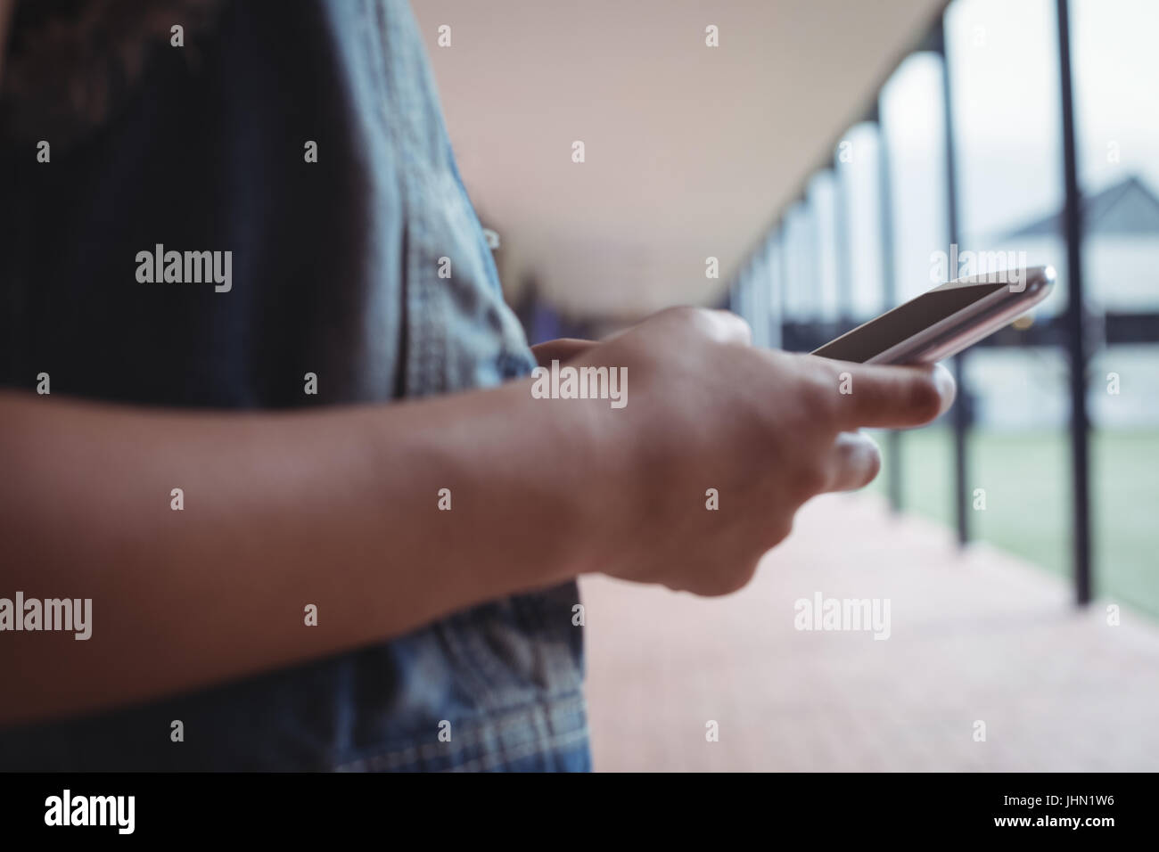 Mid section of girl using mobile phone while standing in corridor at ...
