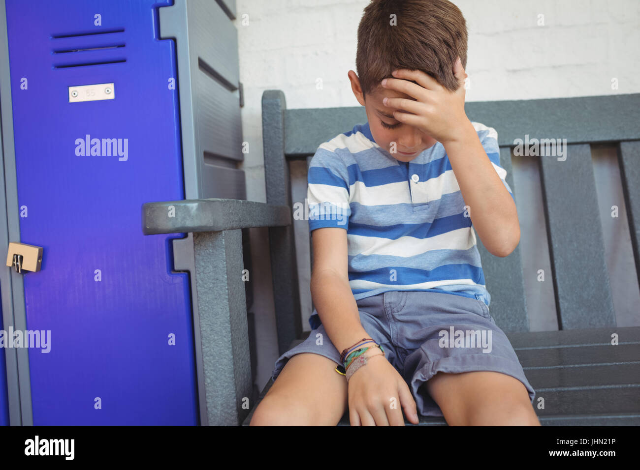 Sad boy sitting on bench by locker at school Stock Photo - Alamy