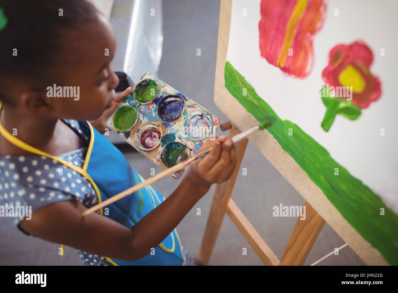 High angle view of elementary girl painting on canvas in classroom ...