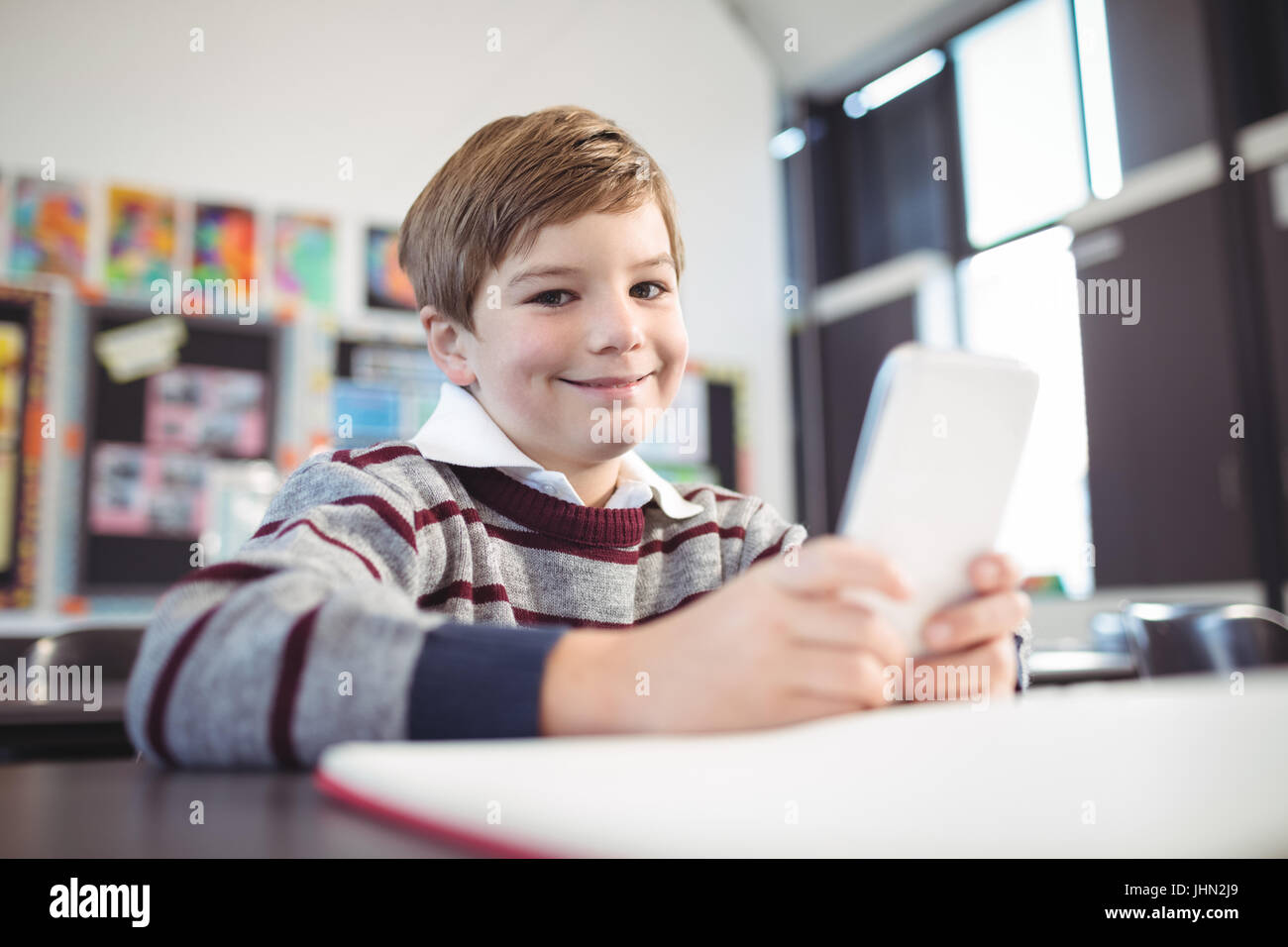 Portrait of smiling boy using mobile phone at desk in school Stock ...