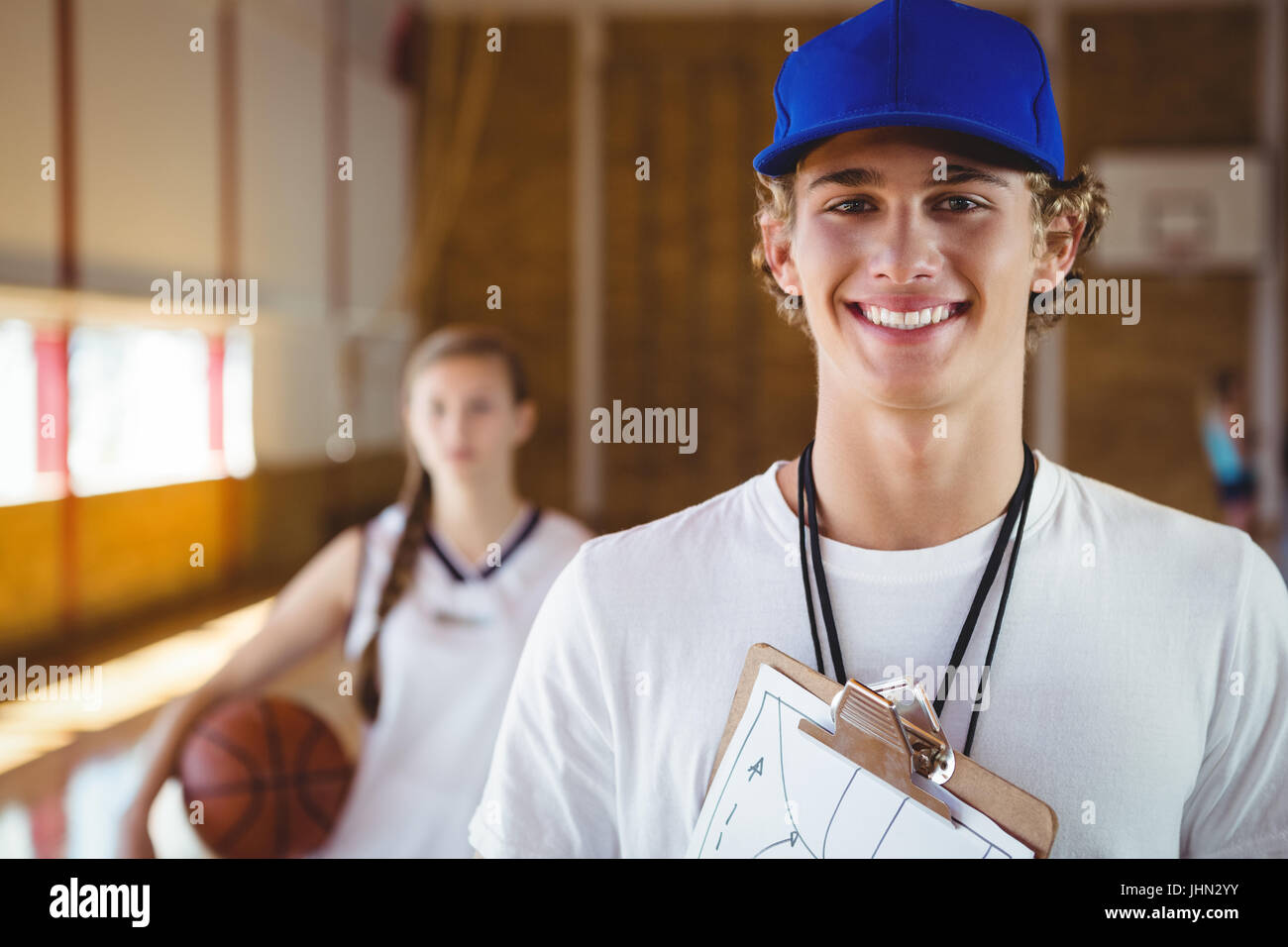 Portrait of smiling male coach with basketball player standing in court ...