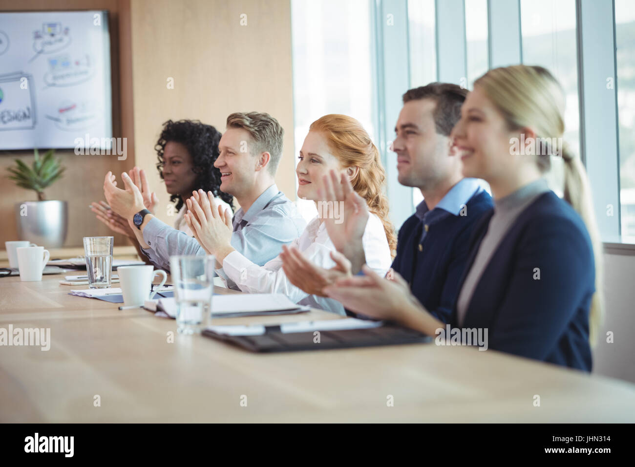 Happy business people clapping at conference table during meeting in ...