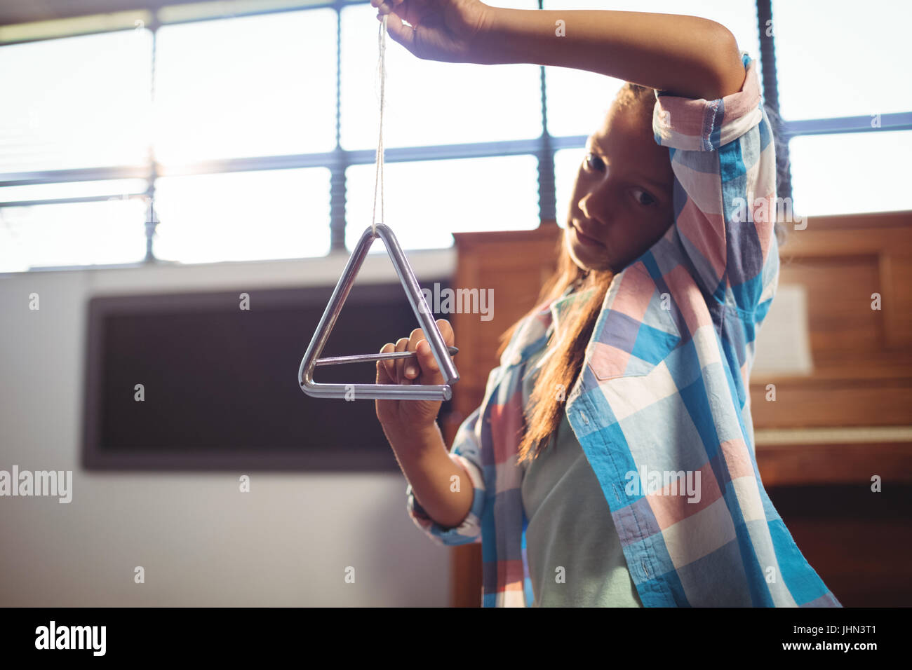 Portrait of girl playing triangle in classroom at music school Stock ...