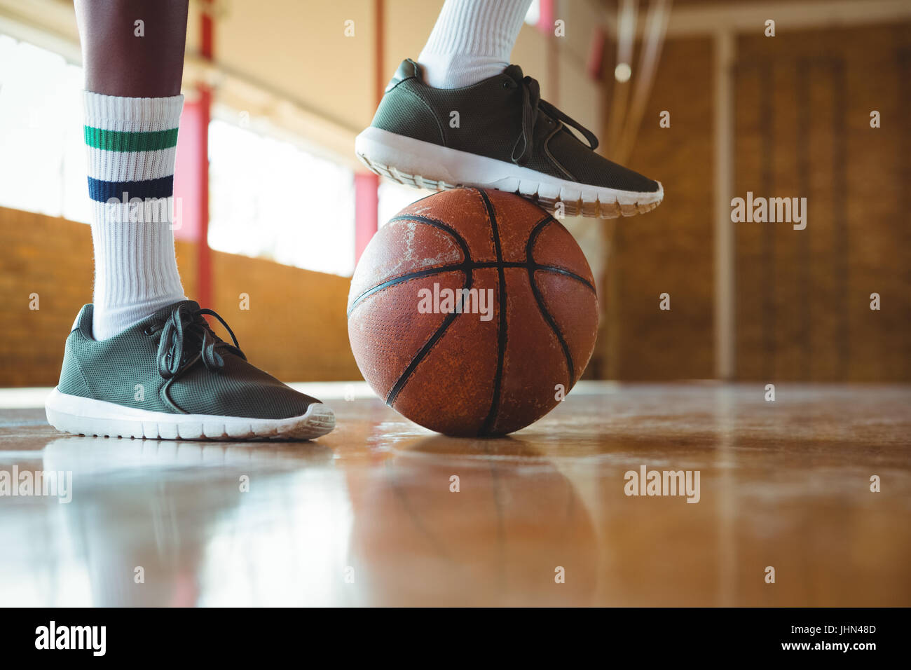 Low section of male teenager stepping on basketball while practicing in ...