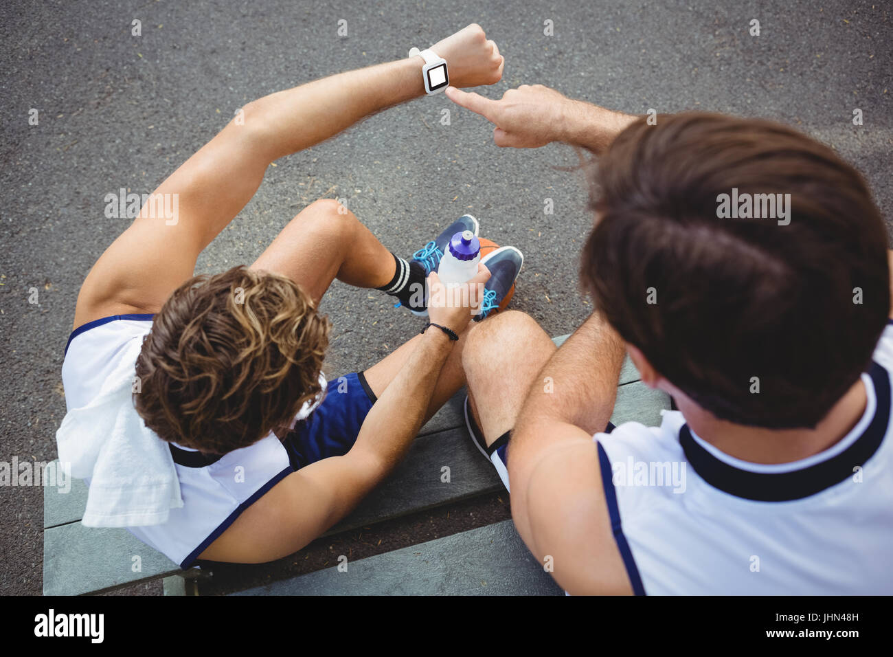 Overhead view of basketball players looking at smartwatch while sitting ...